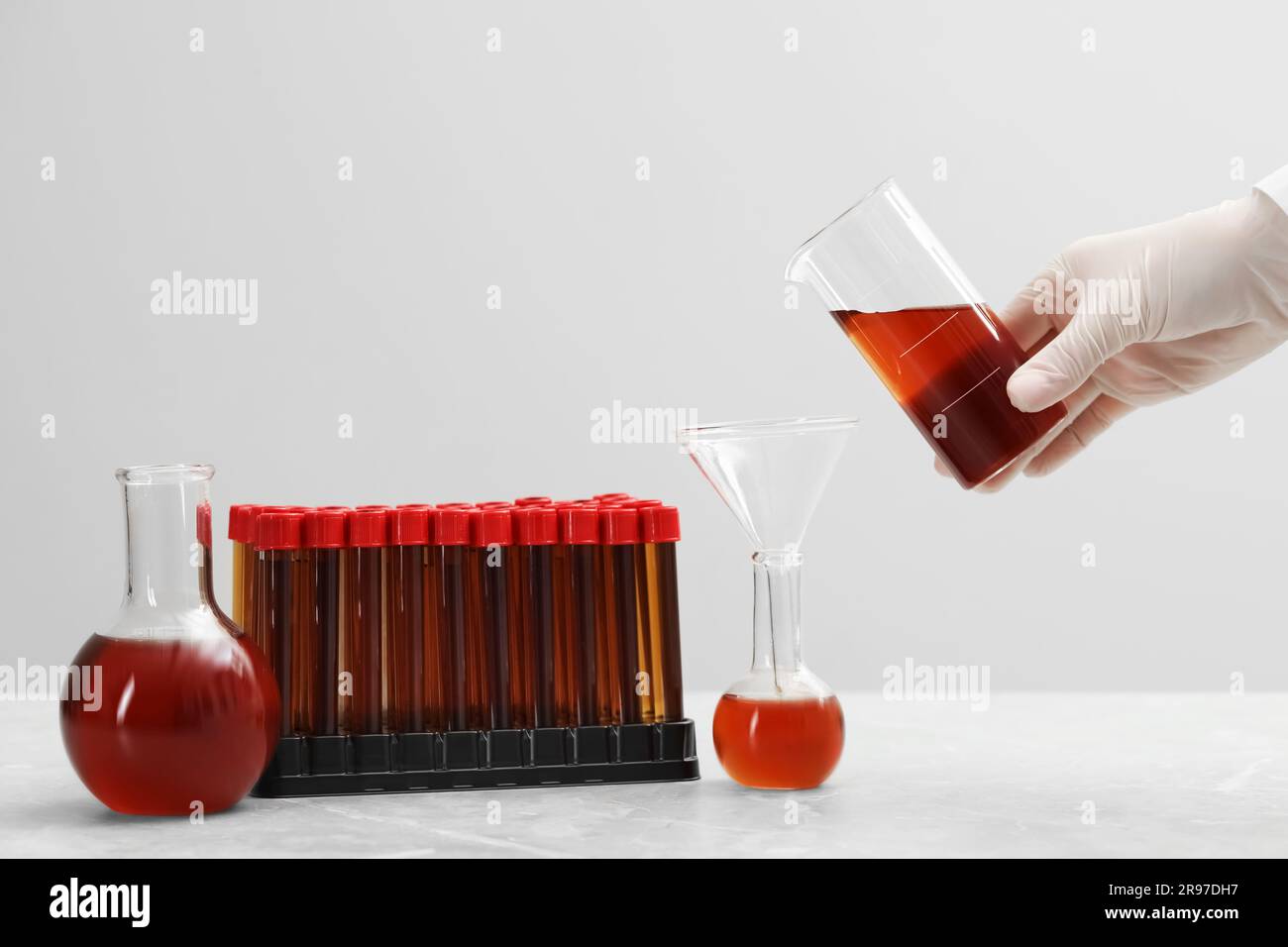 Scientist pouring liquid from beaker into conical flask on white table ...