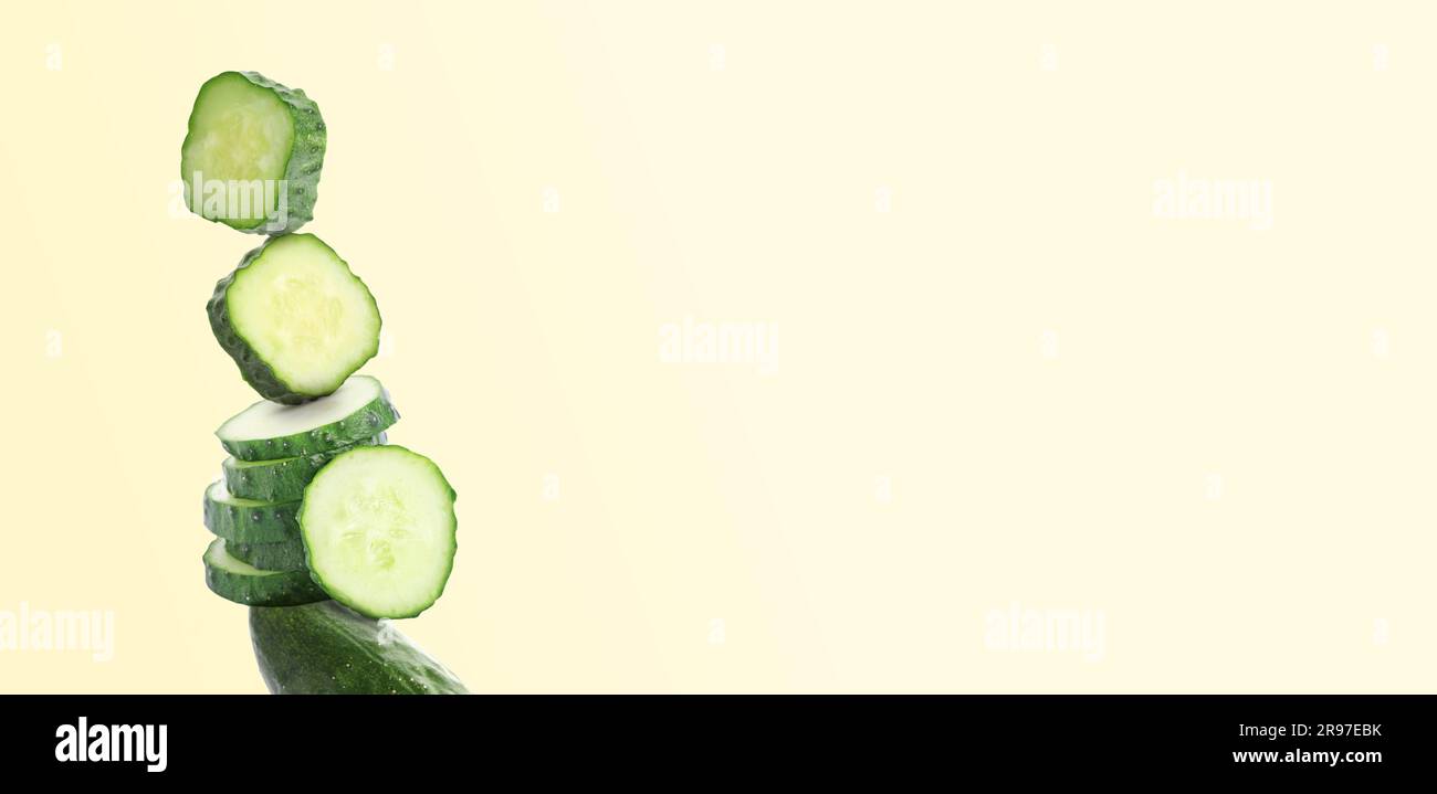 Cut and whole fresh cucumbers on pale light yellow gradient background ...