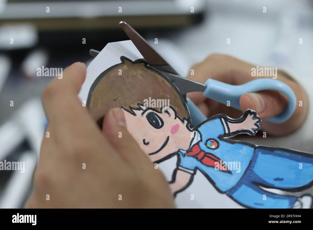 A close-up of a young student carefully cutting out their drawing of a ...