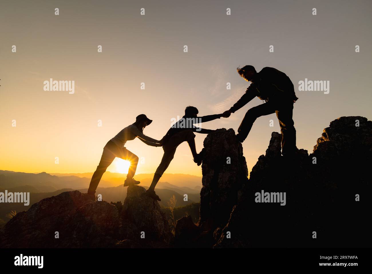 Silhouette of Hikers climbing up mountain cliff. Climbing group helping ...