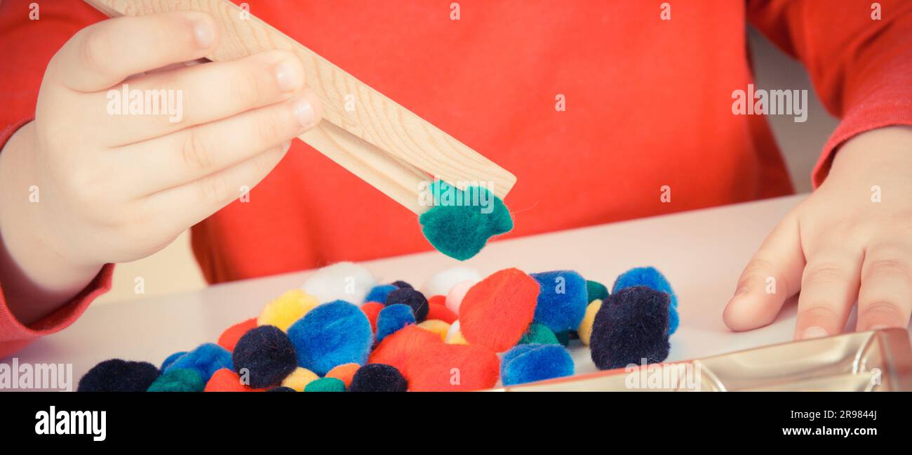 Preschooler playing with small colorful pompoms and wooden tongs ...