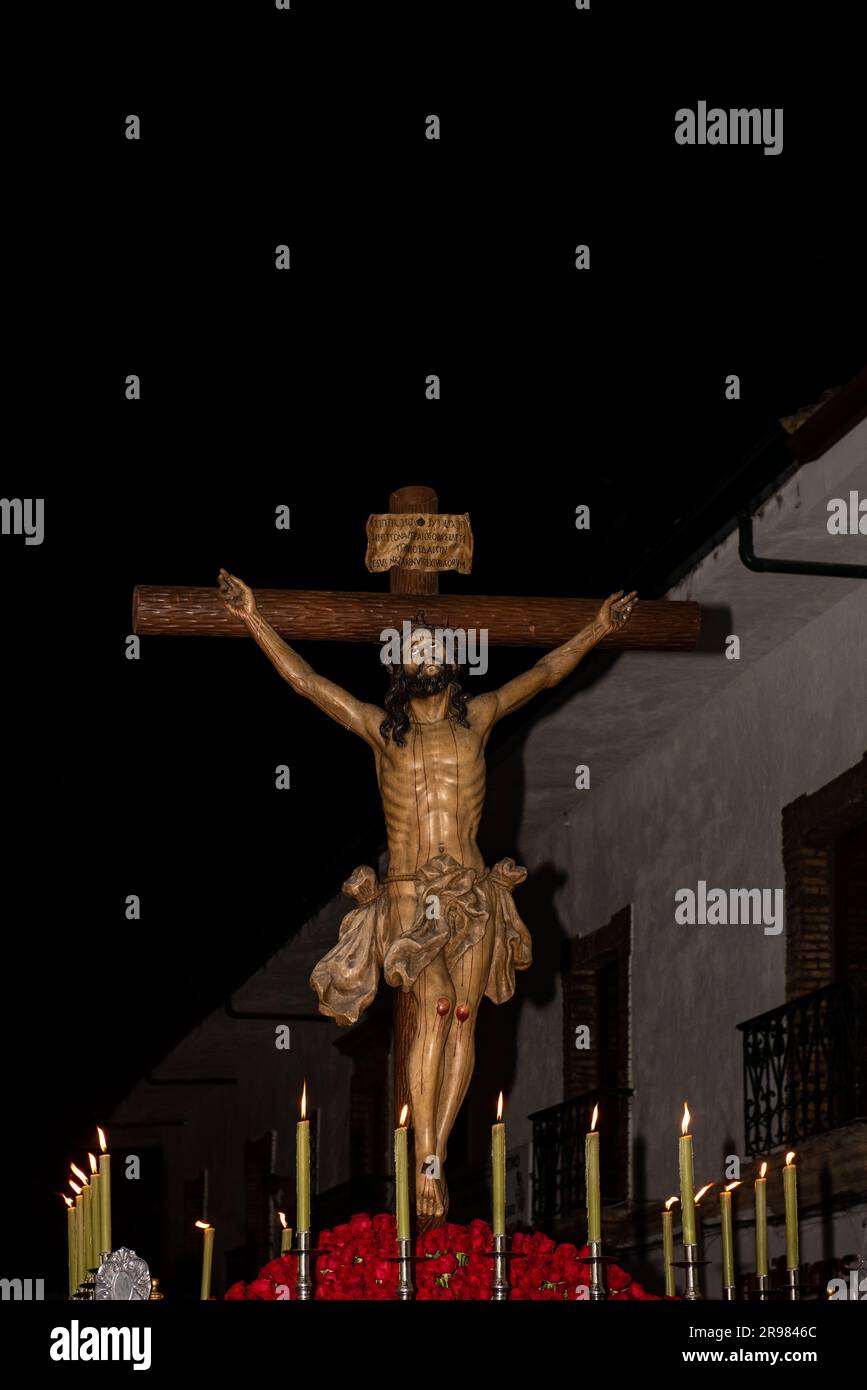 A statue of Jesus Christ hangs on the cross at night with lit candles ...