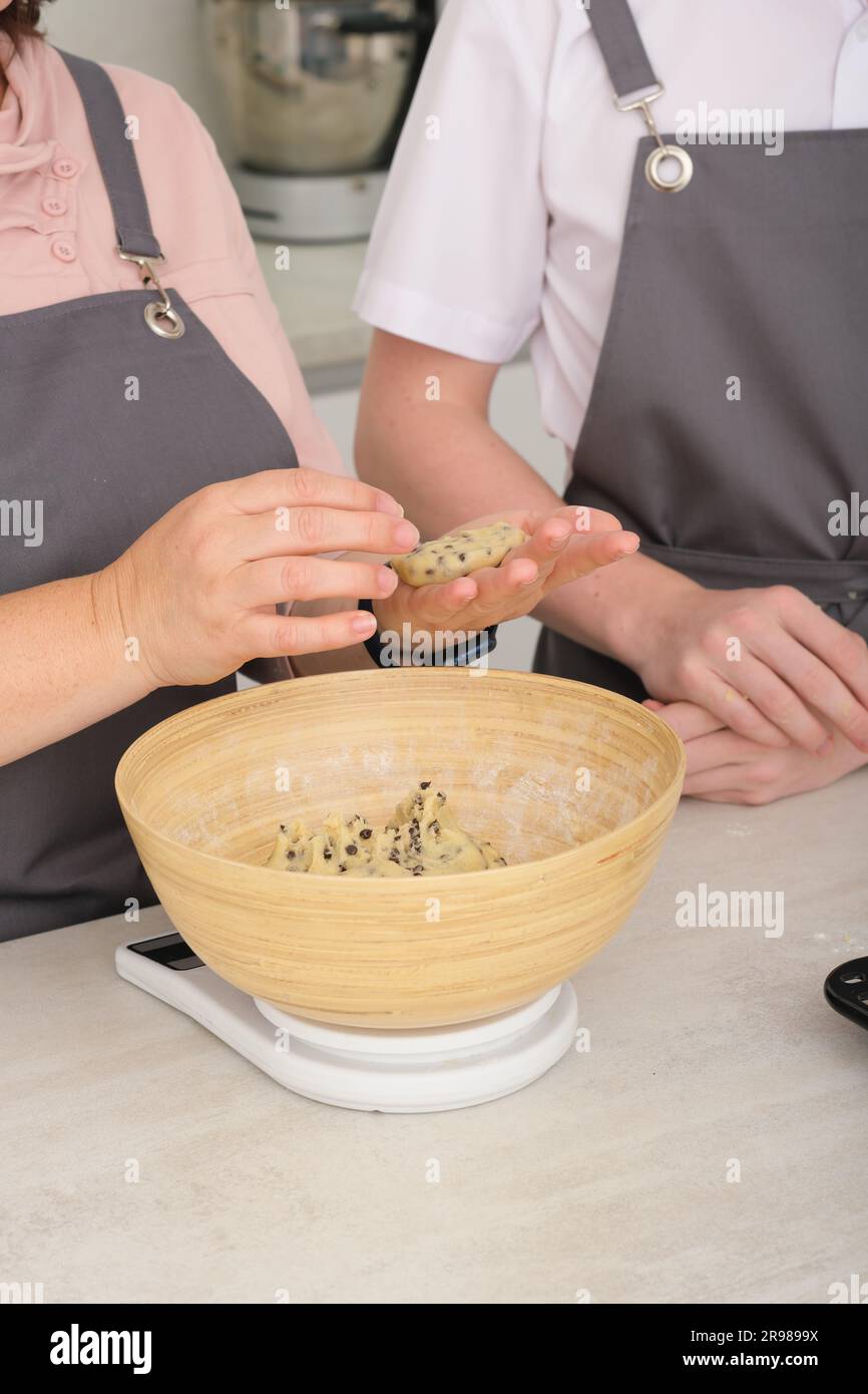 woman chef making dough for chocolate cookies teaching young male chef ...