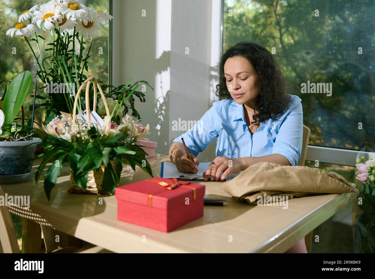 Female florist writes notes on clipboard, draws composition of flowers ...
