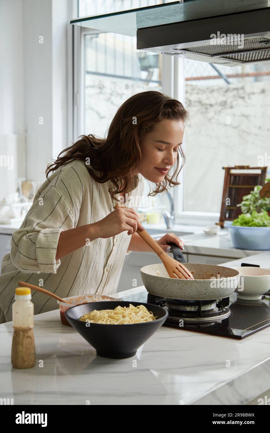 Young woman enjoying delicious smell of spaghetti sauce she is making ...