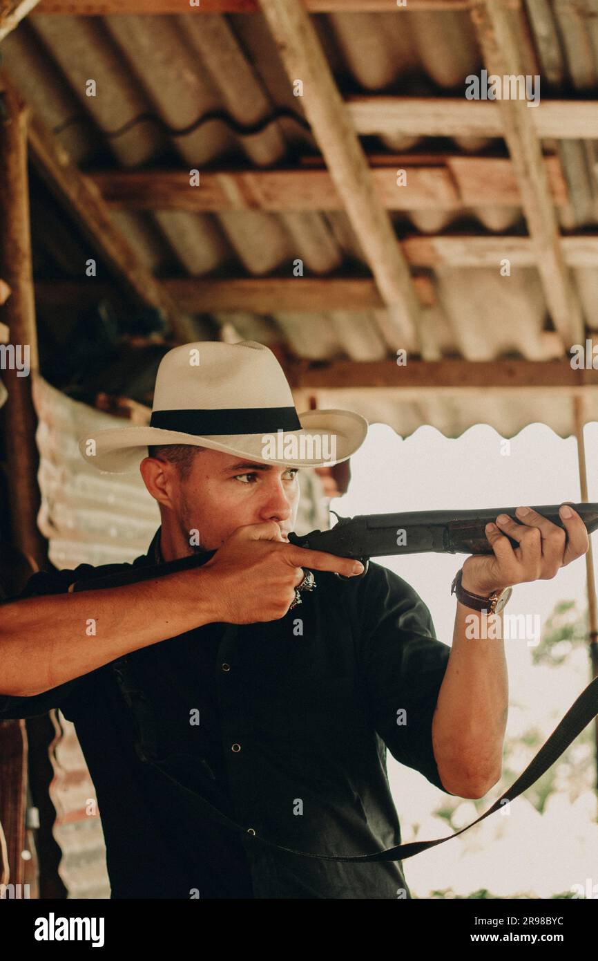 A Caucasian male stands beneath a sheltered structure, wearing a hat ...