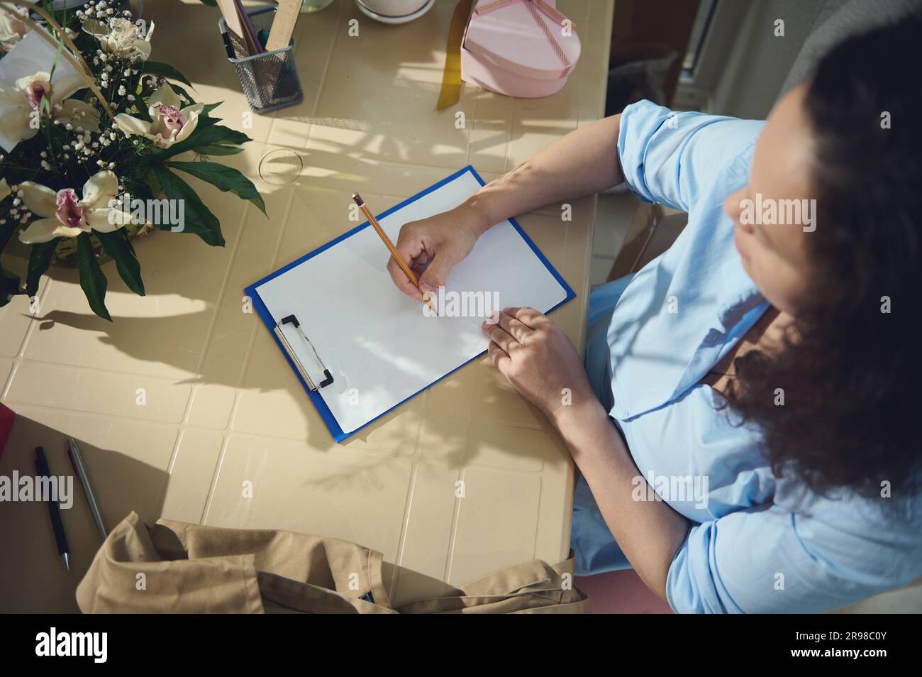 Directly above female entrepreneur florist holding a pencil, writing ...