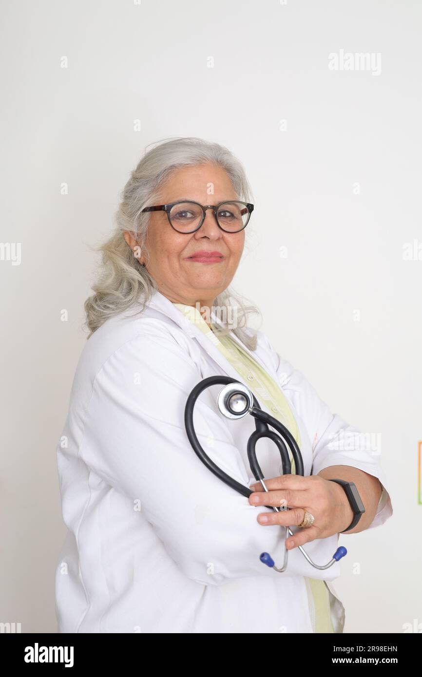 Senior female doctor in lab coat with arms crossed against white ...