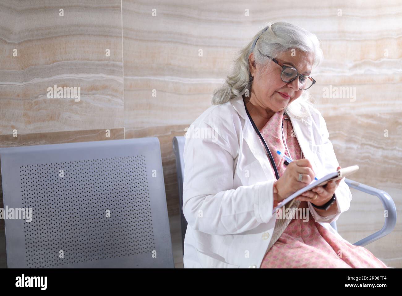 Portrait of smart senior female doctor in white lab coat sitting on ...