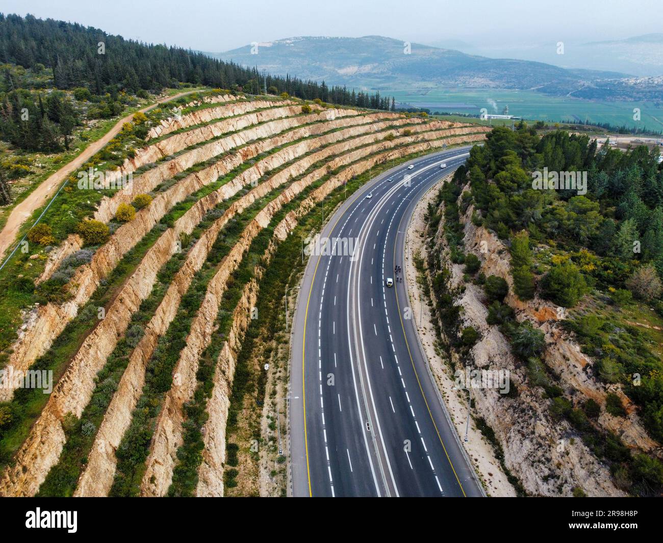 A scenic winding road passing through a tranquil valley with lush green ...