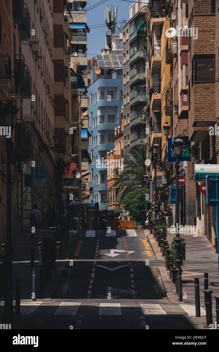 A narrow city street in Alicante, Spain, featuring tall buildings and ...