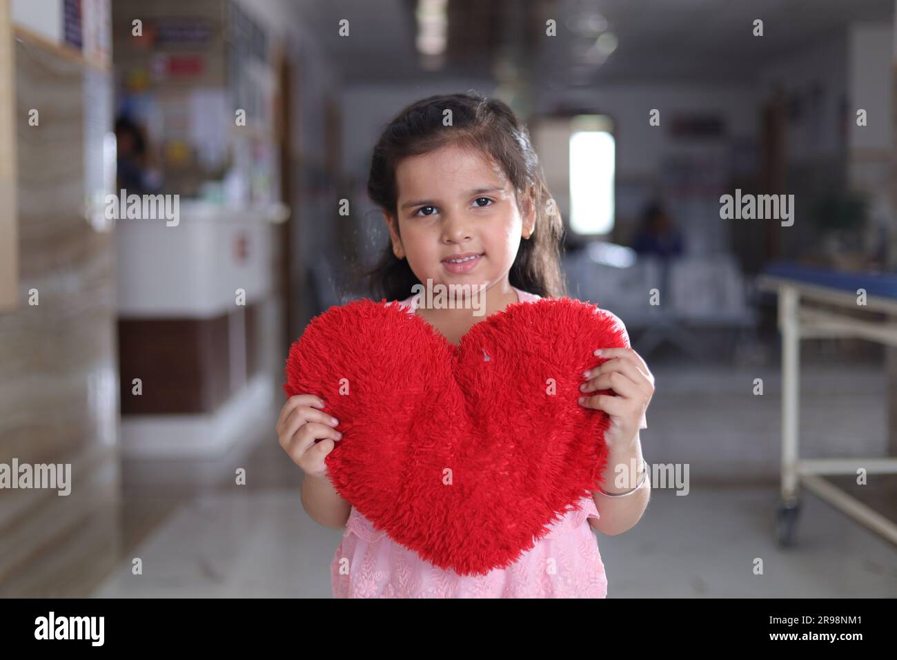 Small girl child showing red colored heart shaped cushion, standing in ...