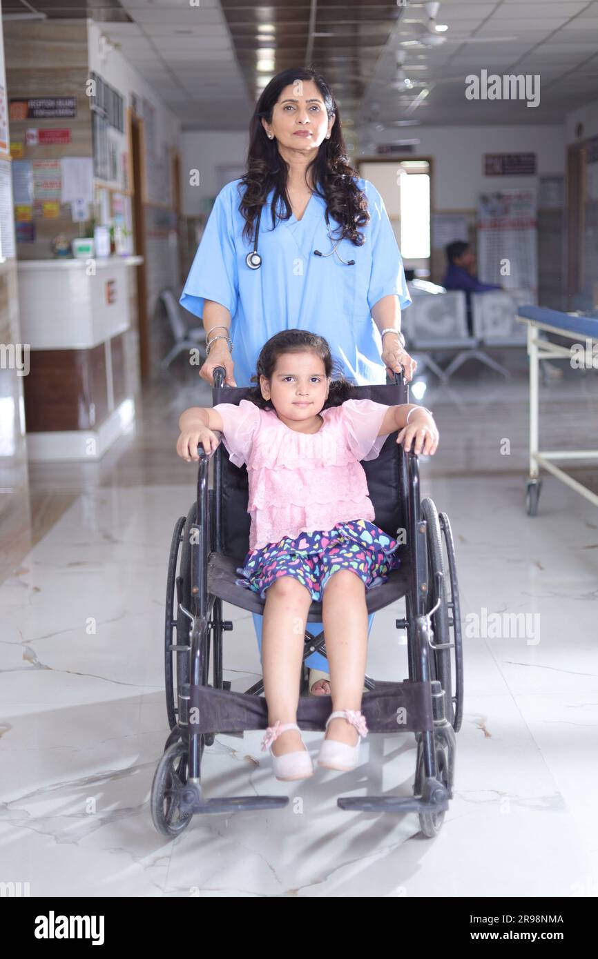 small girl child sitting on a wheelchair with a nurse taking care of ...