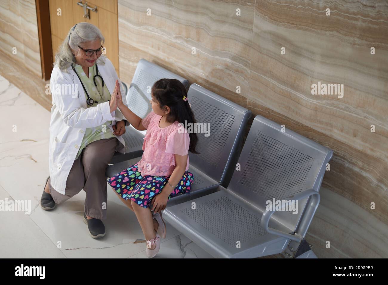 Girl child sitting on bench in hospital corridor, senior doctor giving ...