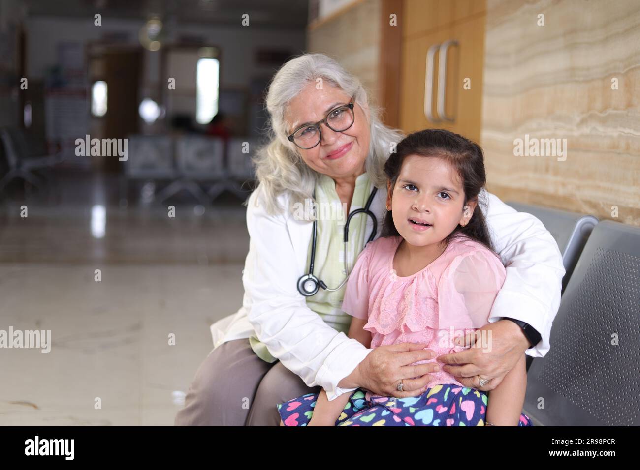 Girl child sitting on bench in hospital corridor, senior doctor giving ...