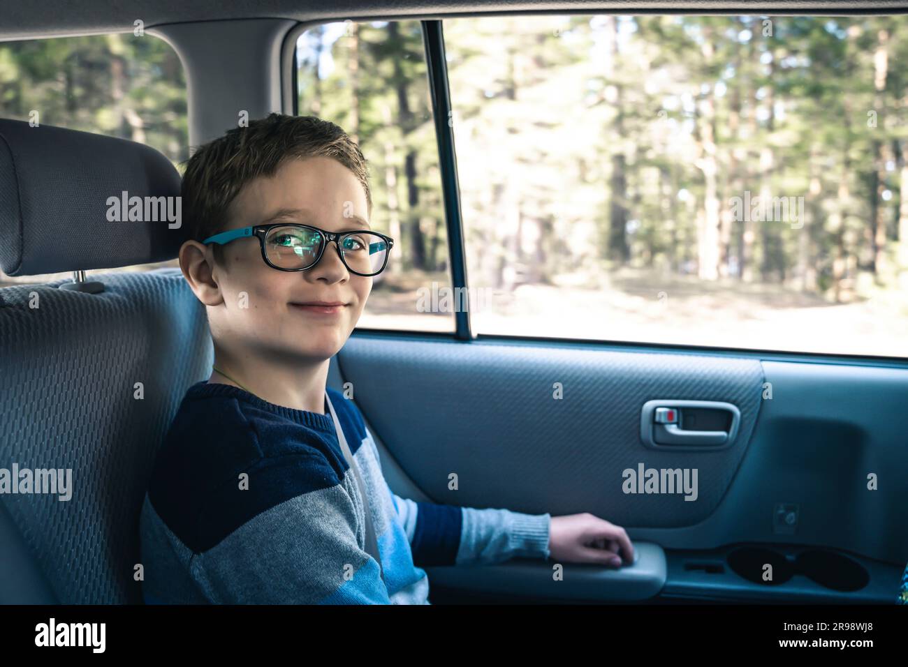 A happy Caucasian boy of school age rides in the back seat of a car and ...