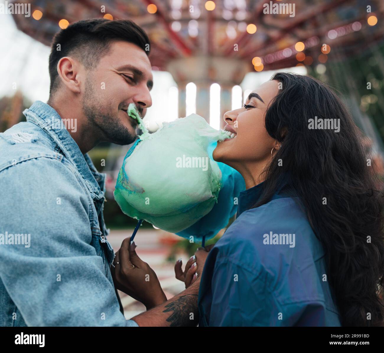 Young happy couple biting cotton candy. Man and his girlfriend bite a ...