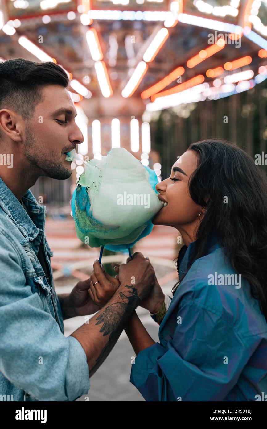 Side view of a young couple eating cotton candy against a carousel ...