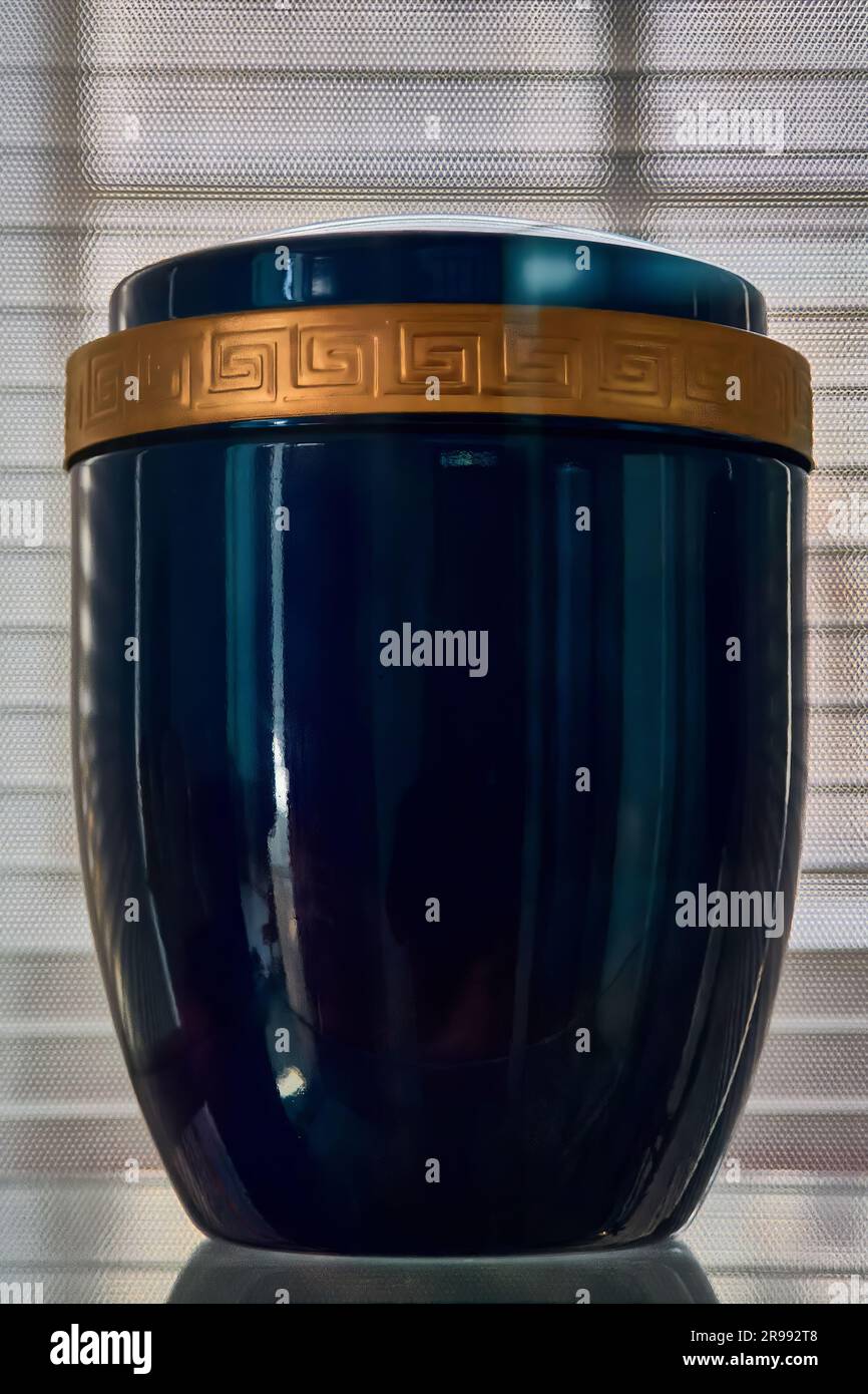 Blue urn for funeral ashes with gold trim, on a shelf with a background ...