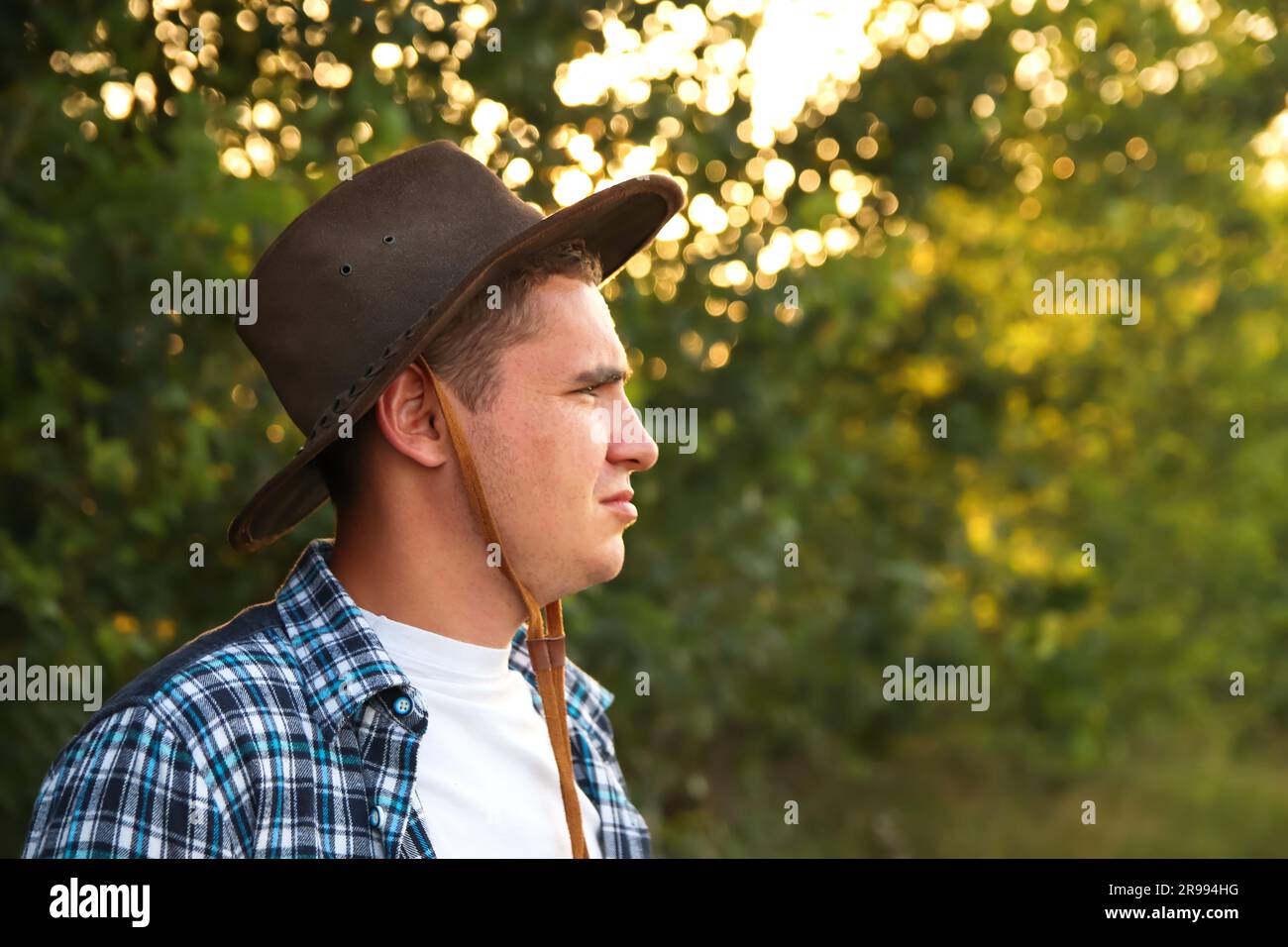 A young farmer in a cowboy hat stands proudly in an agricultural field ...