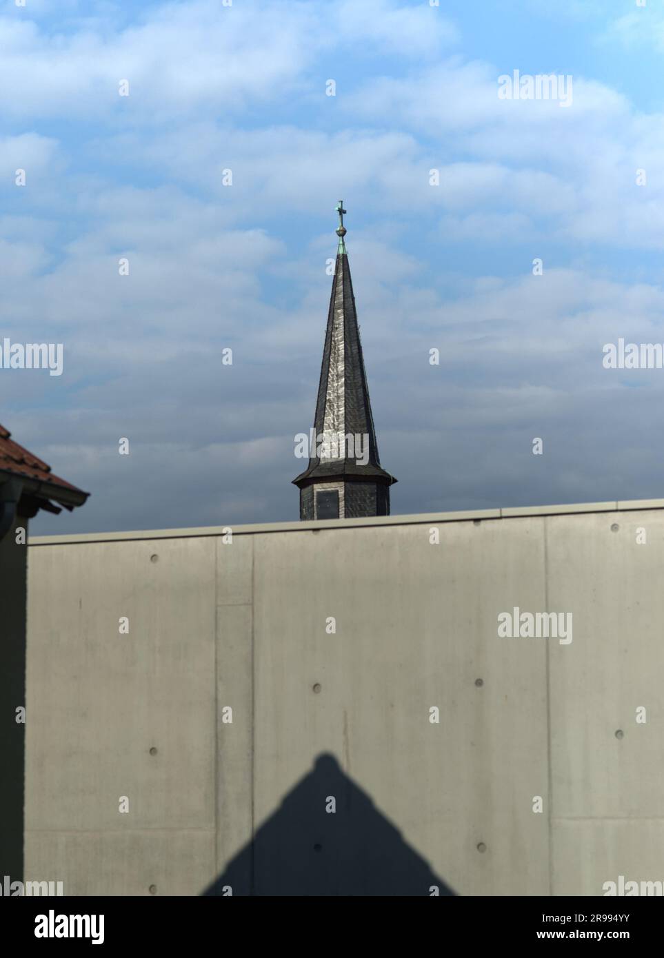 A church spire behind a concrete wall and a roof-shaped shadow on it ...