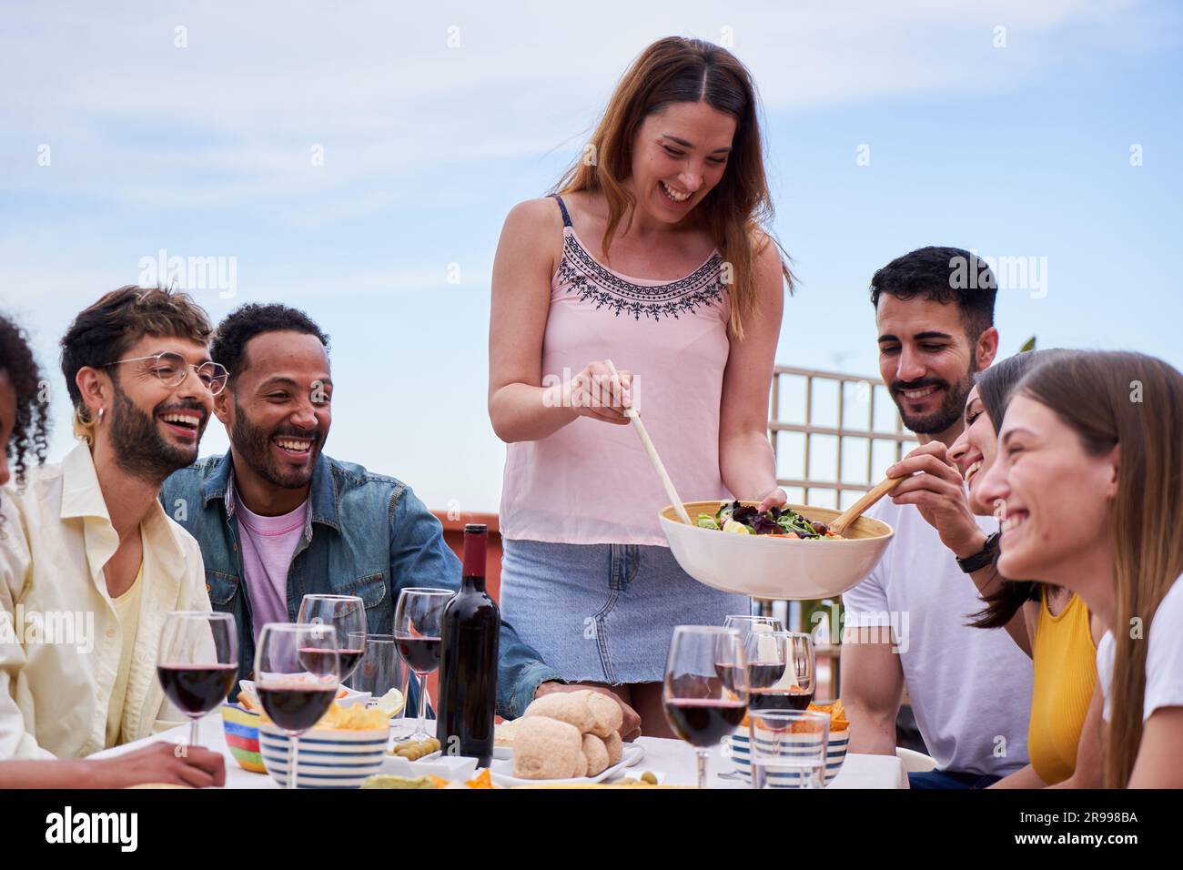 Caucasian woman gathered with her friends, serves salad to her guests ...