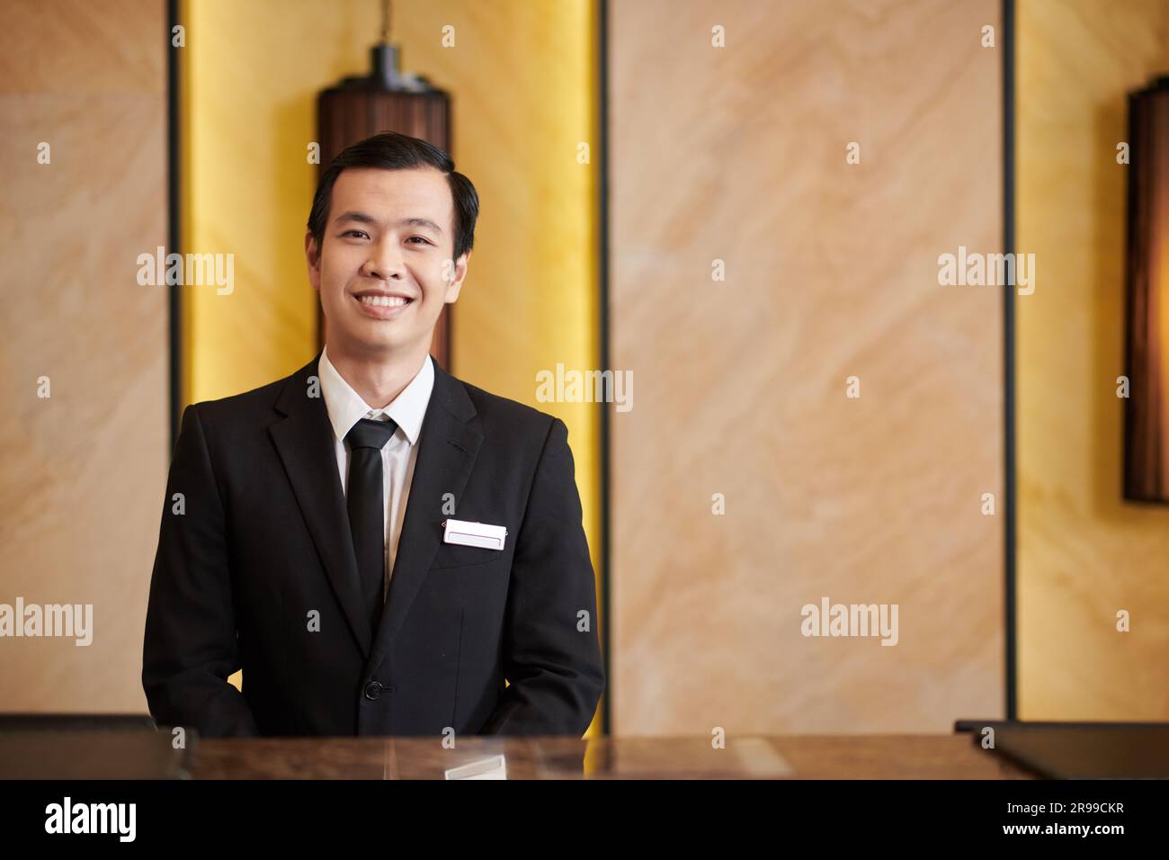Portrait of positive Asian hotel receptionist with badge on his suit ...