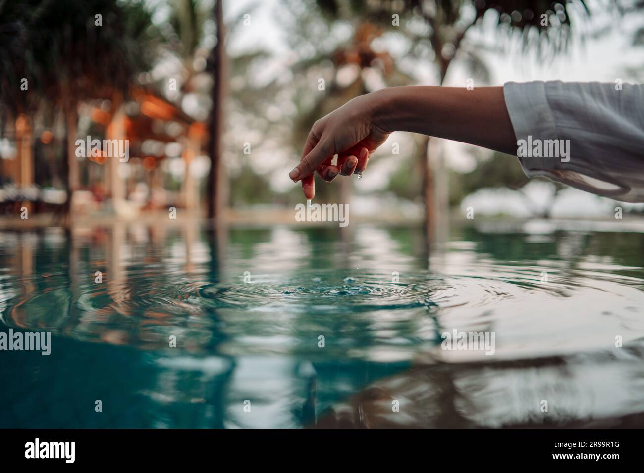 An elegant woman's hand touches the surface of the turquoise water ...