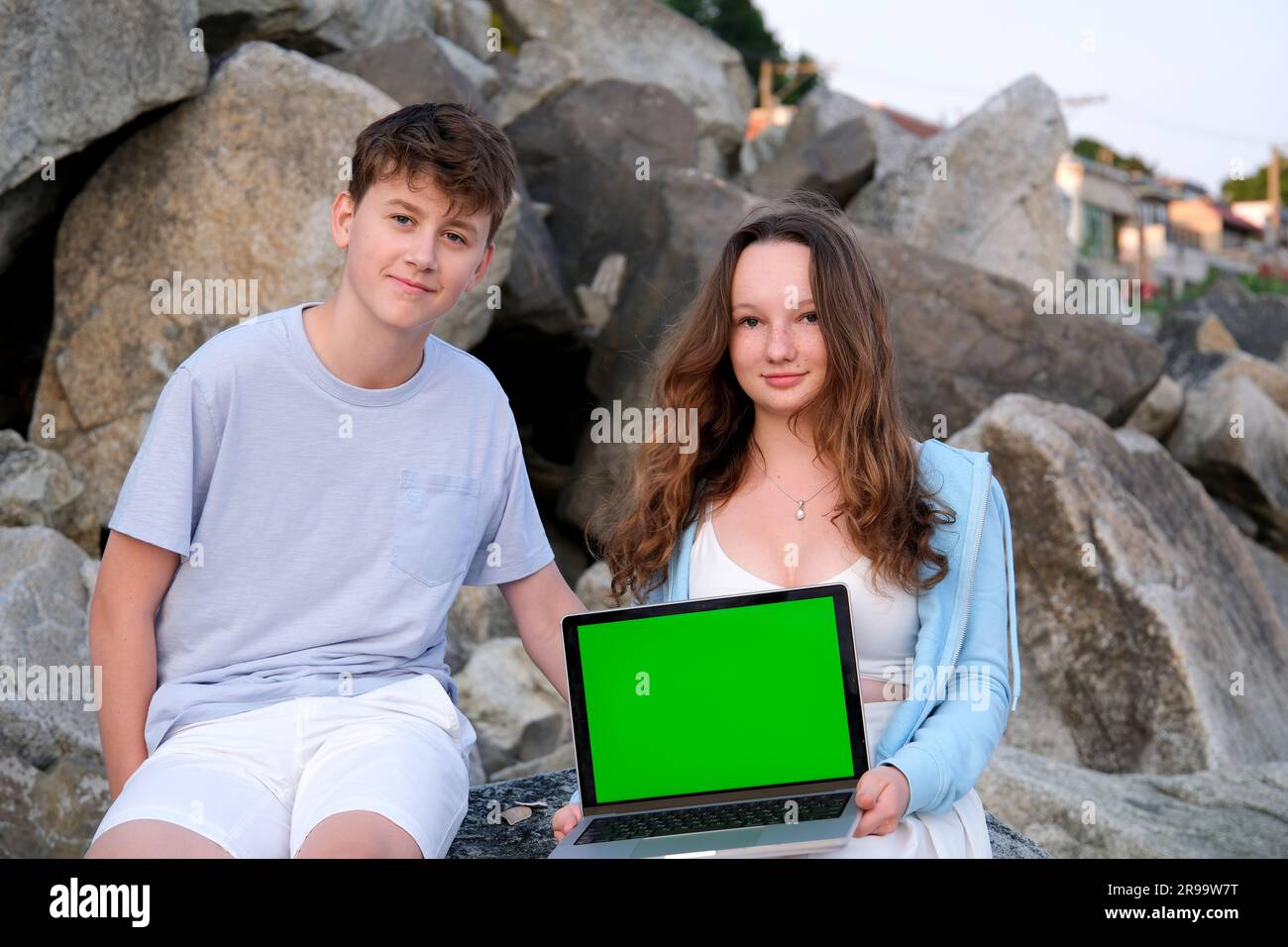 girl and boy teenagers sitting on stones with a laptop in their hands ...
