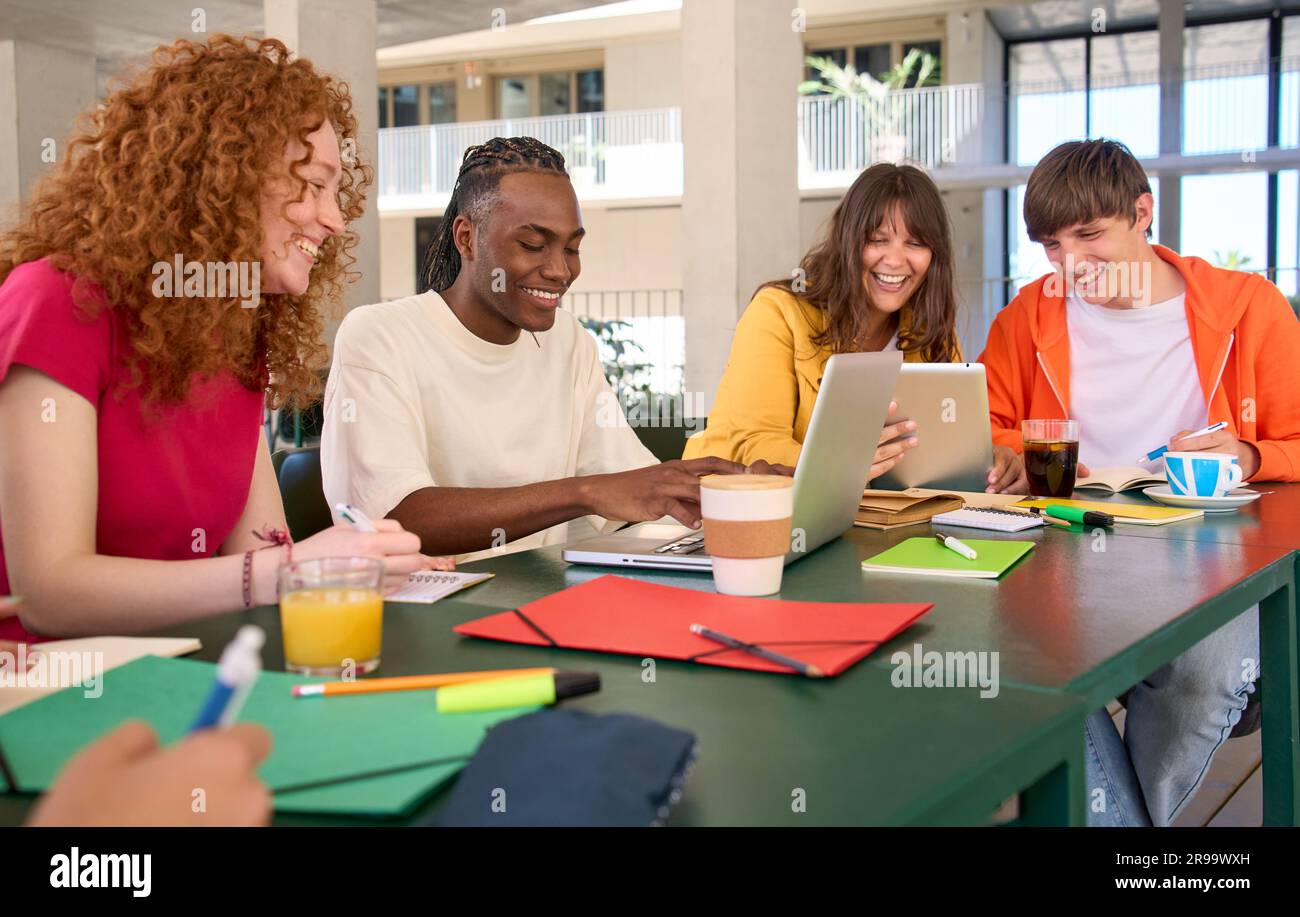 Smiling young people doing homework using laptop tablet in college ...