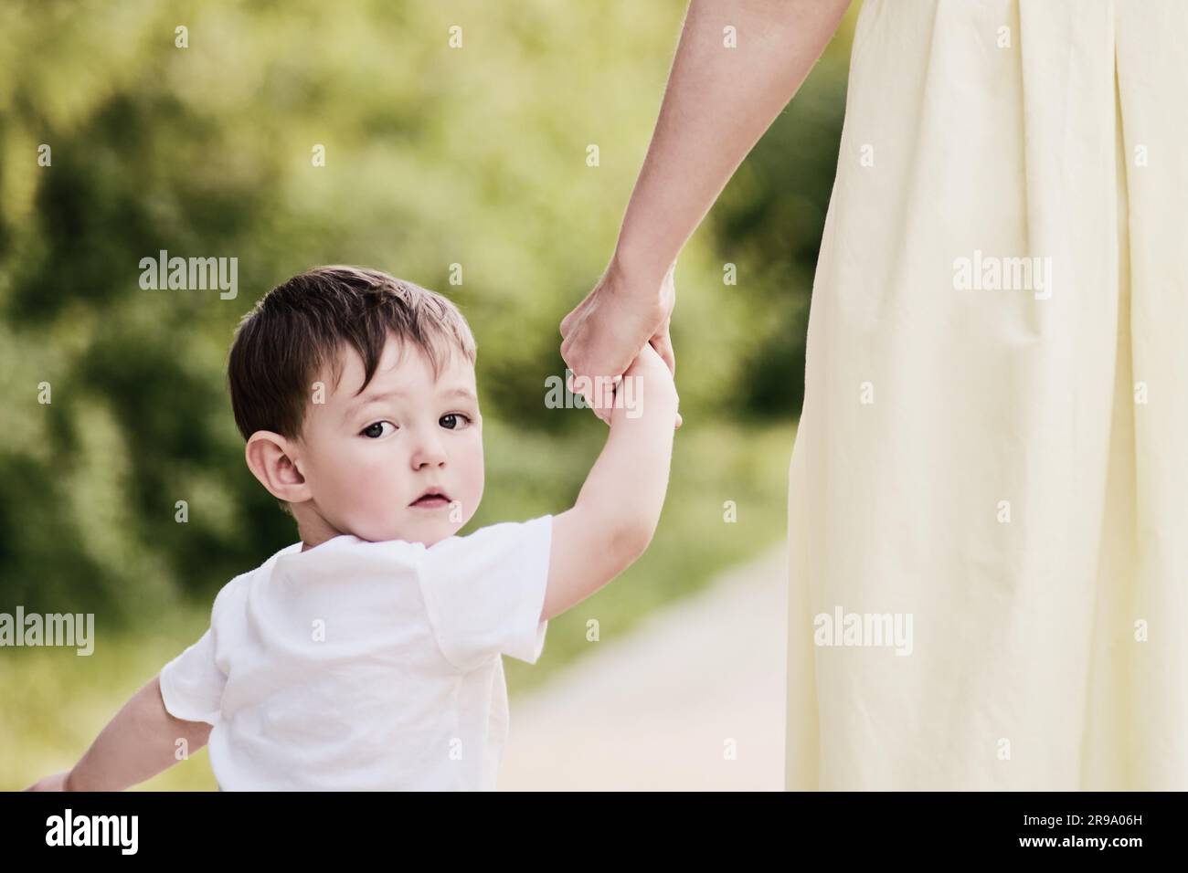 Child boy looks back with fear in his eyes, clutching his mother's hand ...