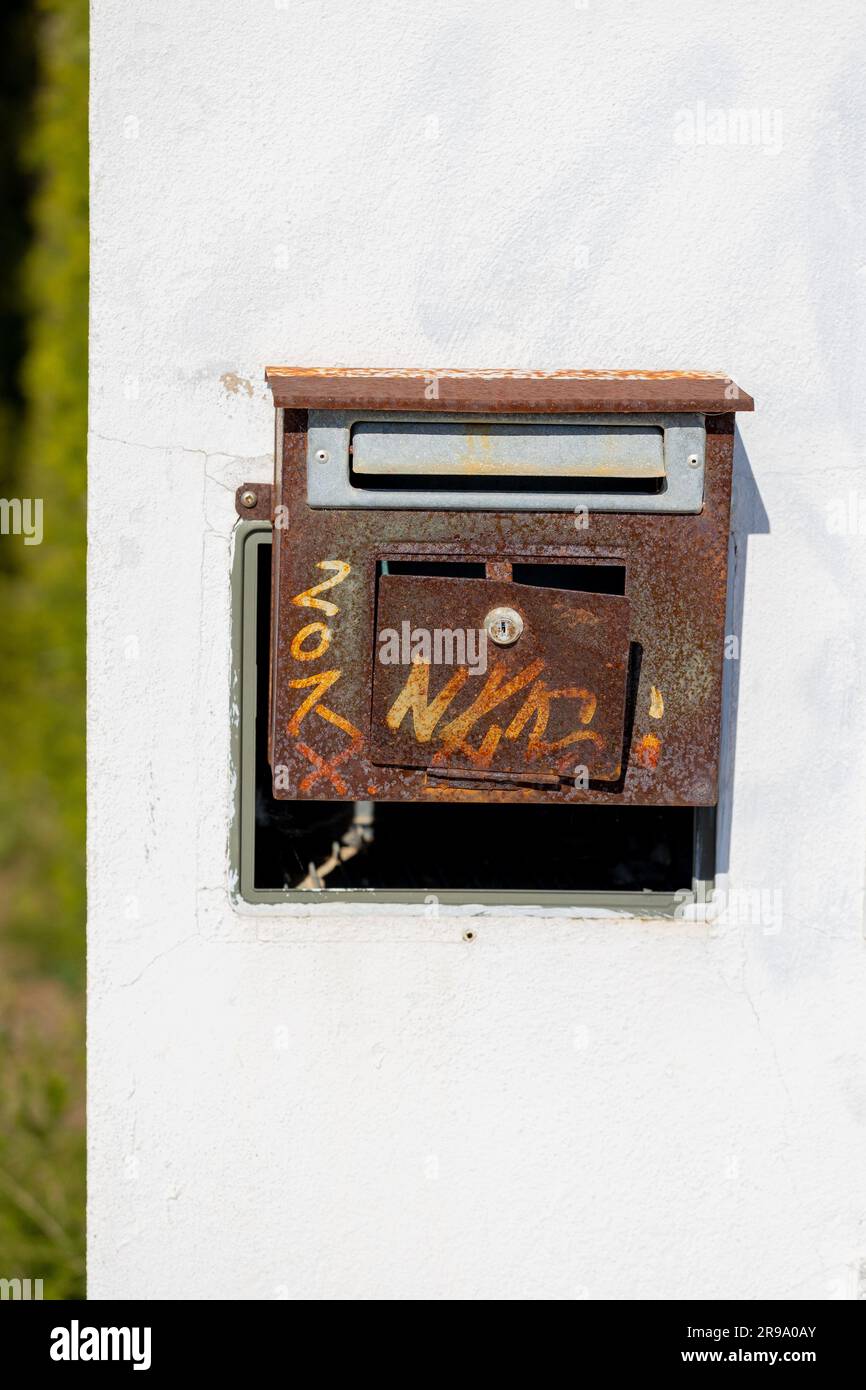 An old, rusty, metal mailbox attached to a white wall in a distressed ...
