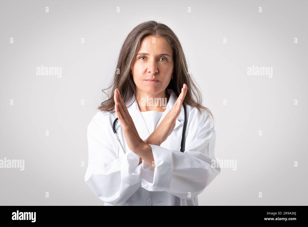 Serious confident senior woman doctor in white coat crossed her arms ...