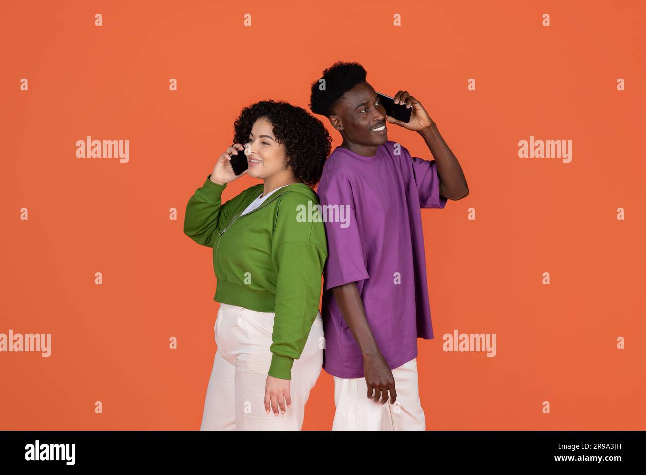 Positive multicultural lovers standing back to back, talking on phones ...