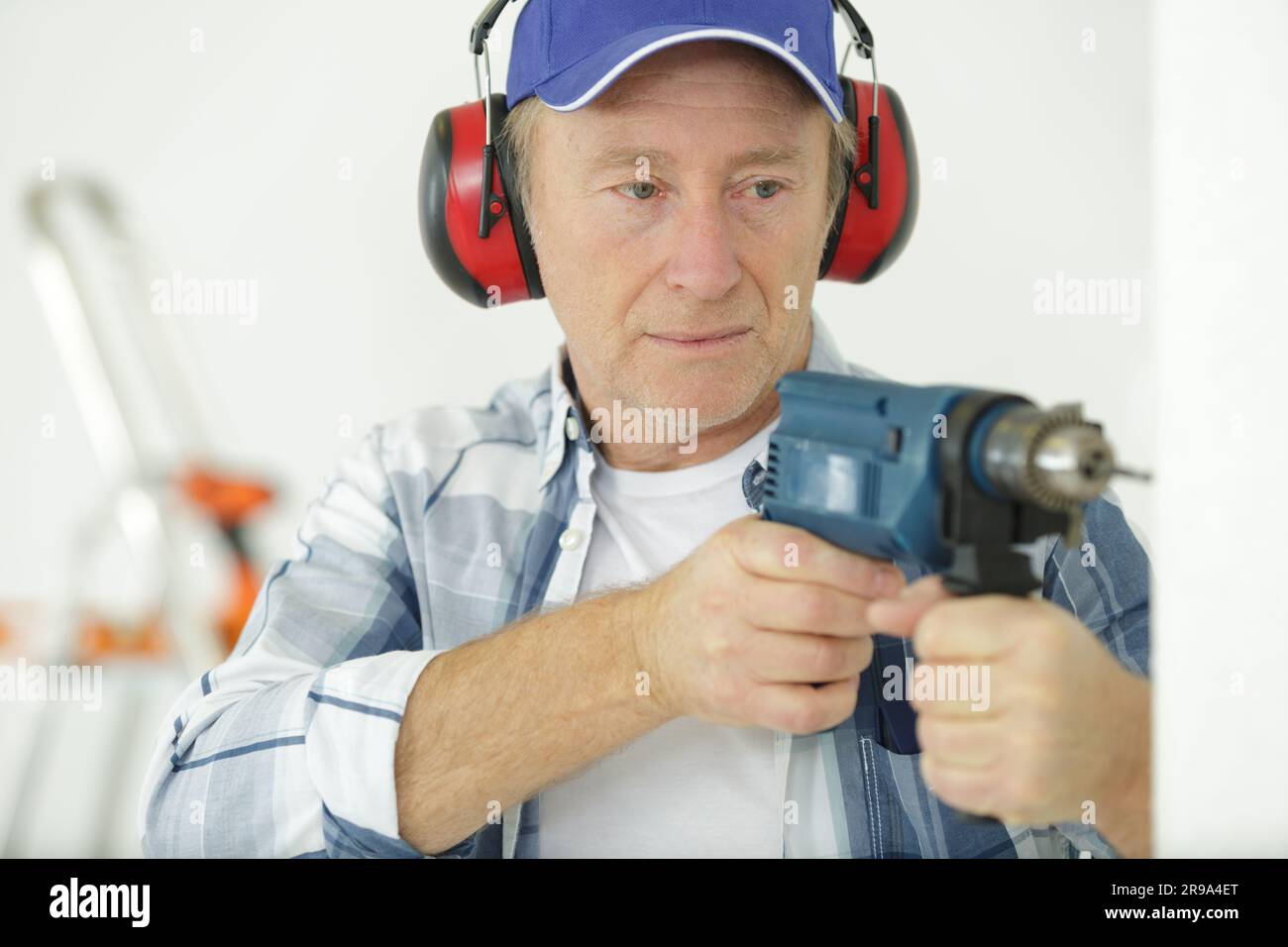 senior workman using drill and wearing ear-defenders Stock Photo - Alamy