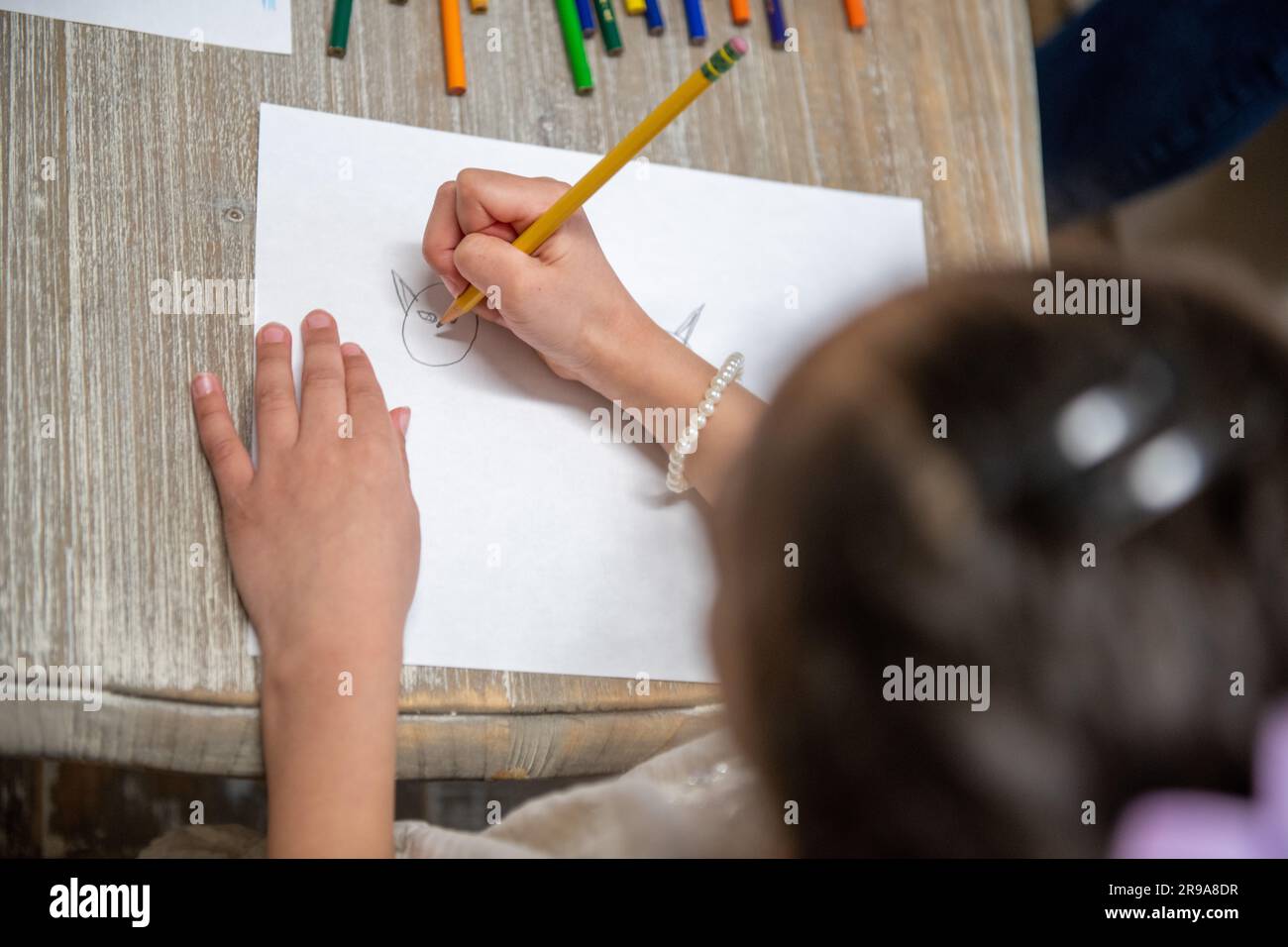 A young female artist sits at a desk while drawing on a peace of paper ...