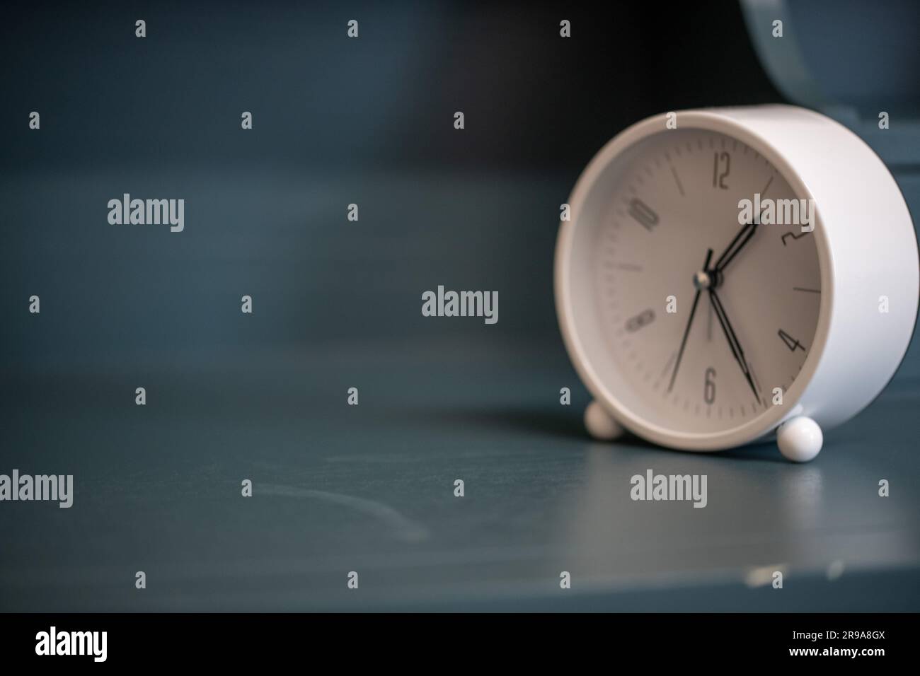 A white alarm clock sitting on a blue shelf, the clock is small in size ...