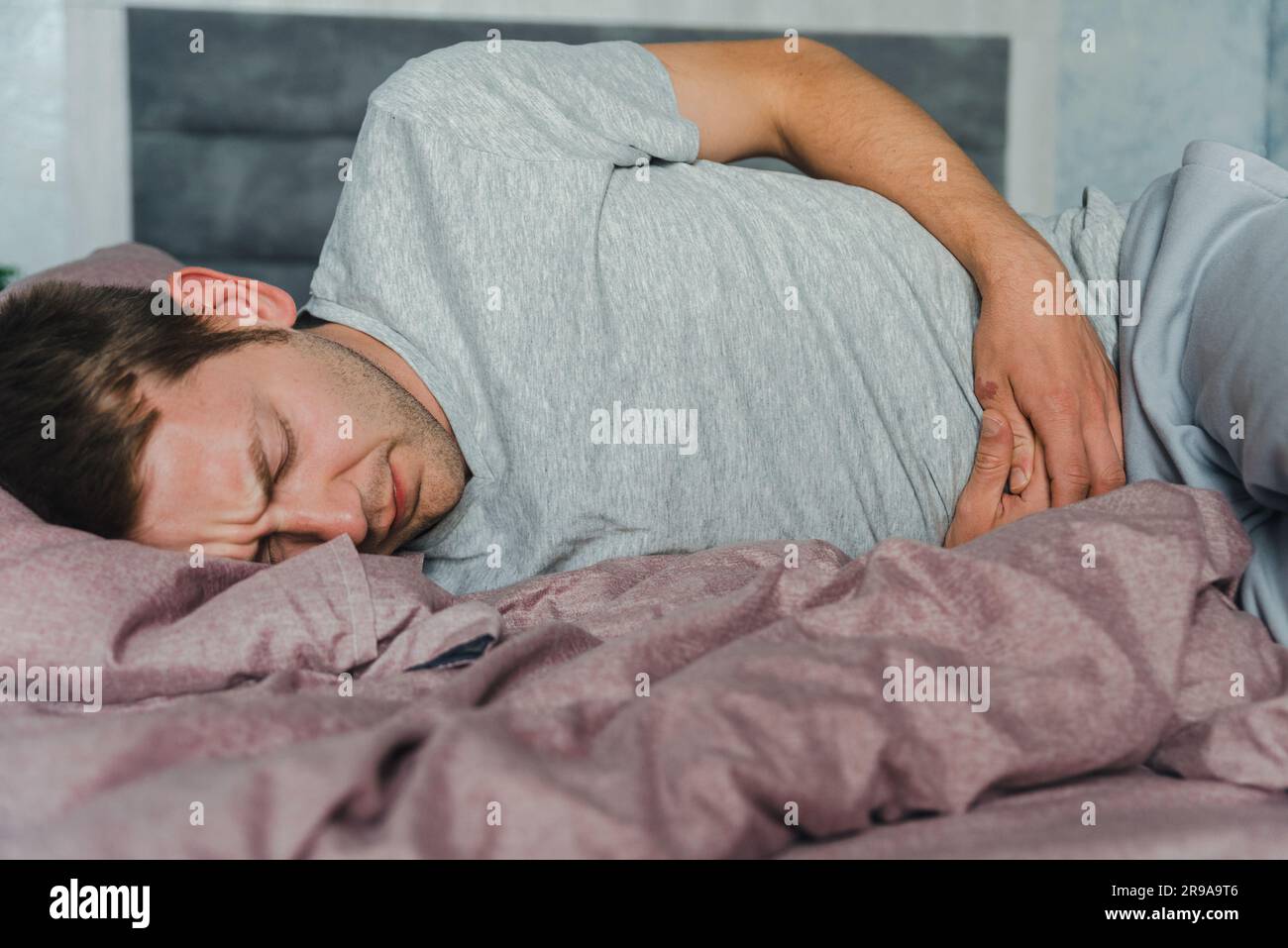 Frustrated handsome young man hugging his belly suffering from stomach ...