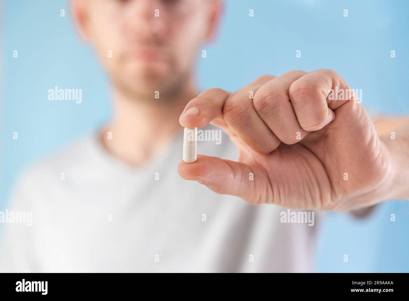 Man hold white capsule with collagen in male hand on blue background. Nutritional supplement ...