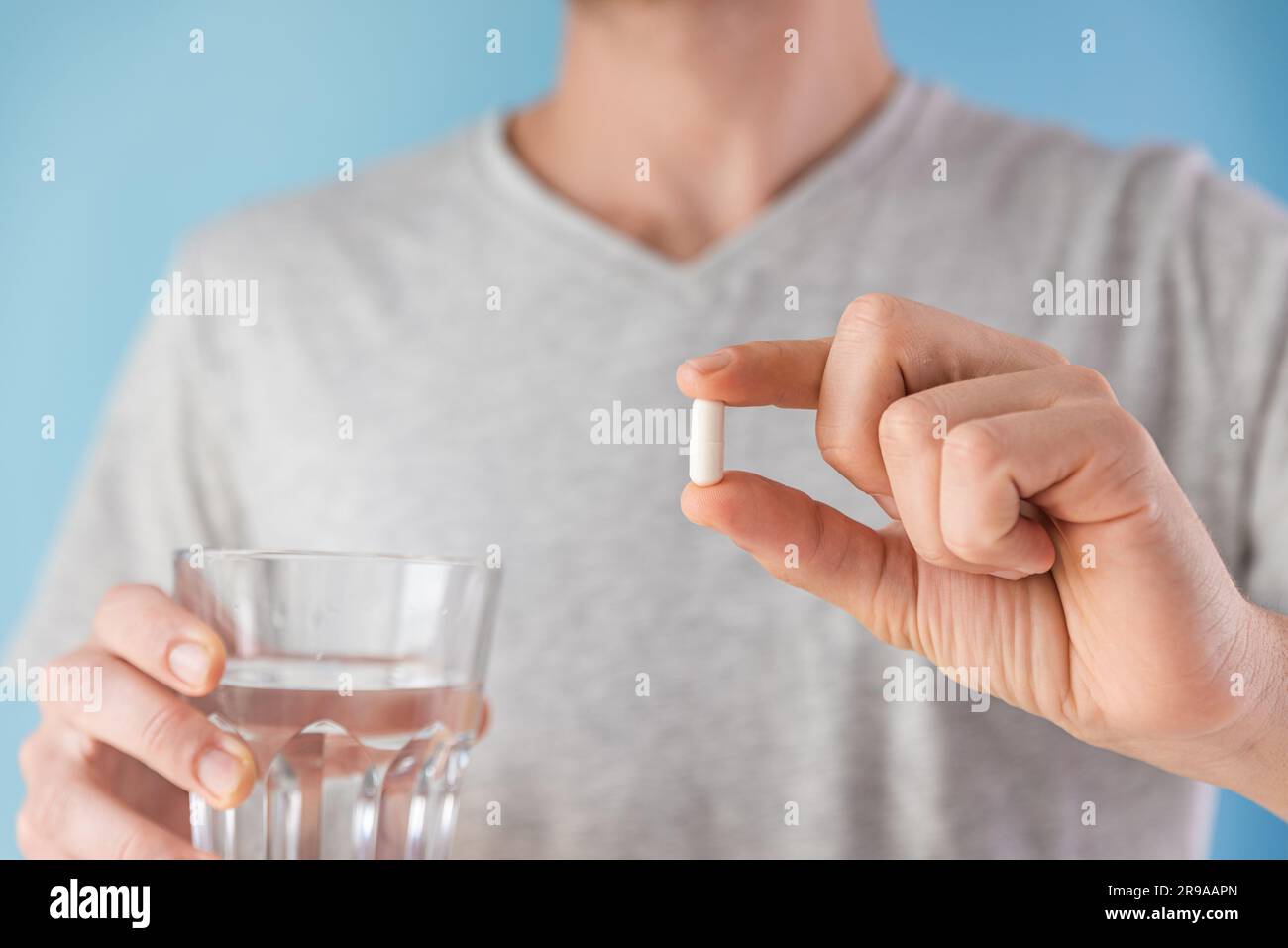Man hold white capsule with collagen in male hand on blue background. Nutritional supplement ...