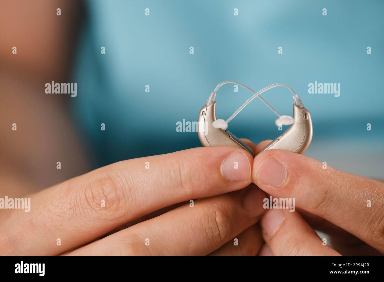 Hearing aids in hands making heart shape over blue background. Closeup ...