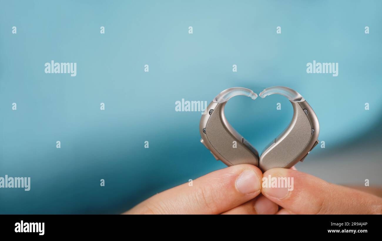 Hearing aids in hands making heart shape over blue background. Closeup ...