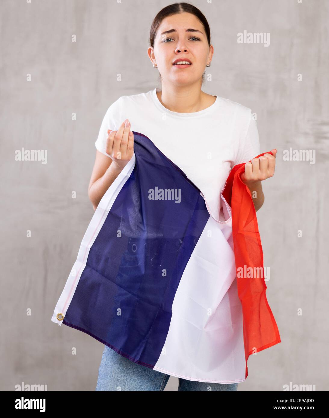 Sad young woman holding France flag against unicoloured background ...