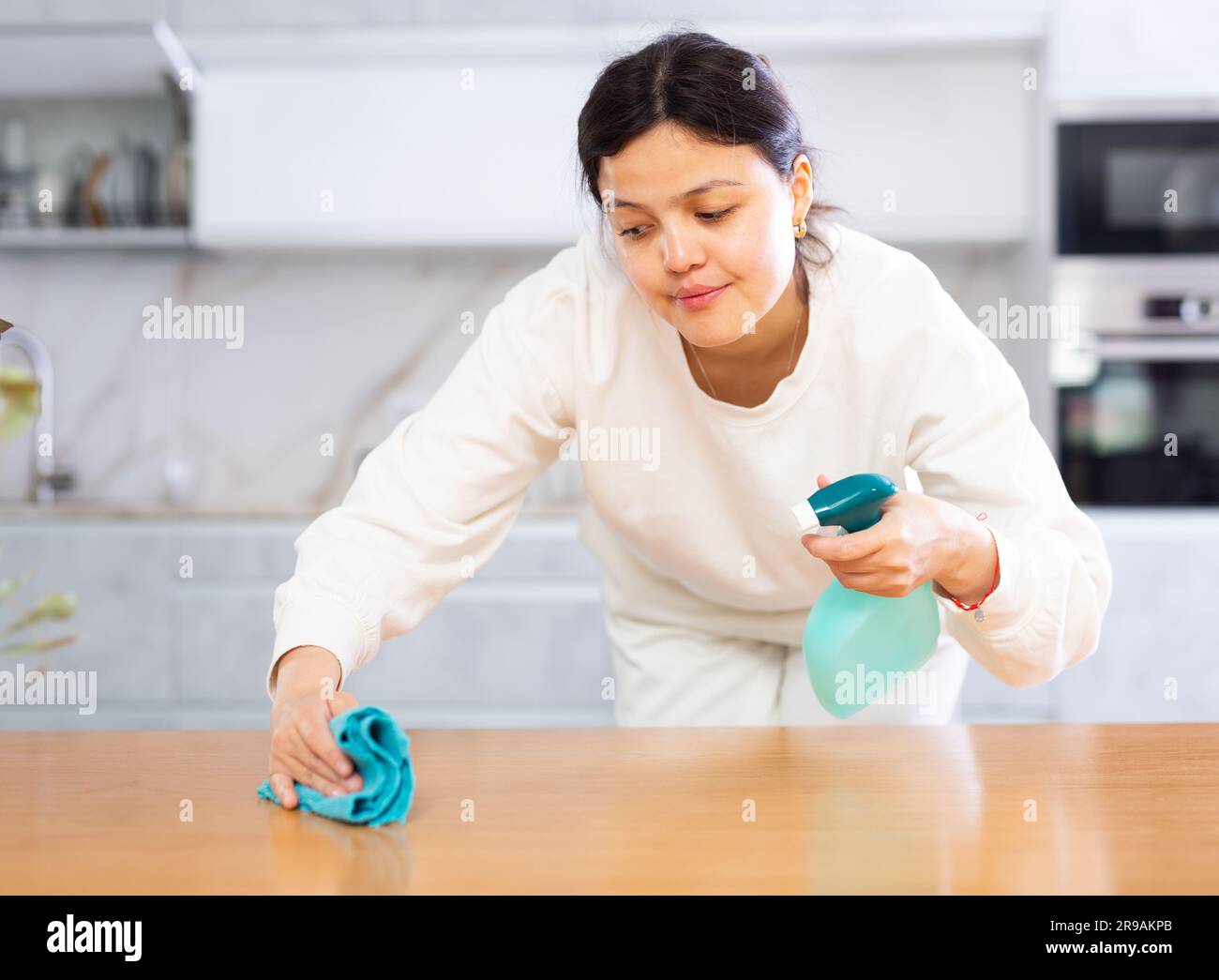 Smiling young woman wiping kitchen countertop with cleaning spray Stock ...