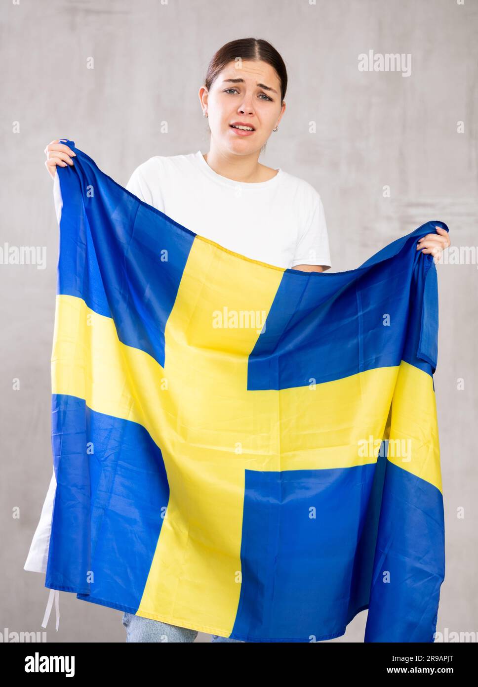 Sad young woman holding Sweden flag against unicoloured background ...
