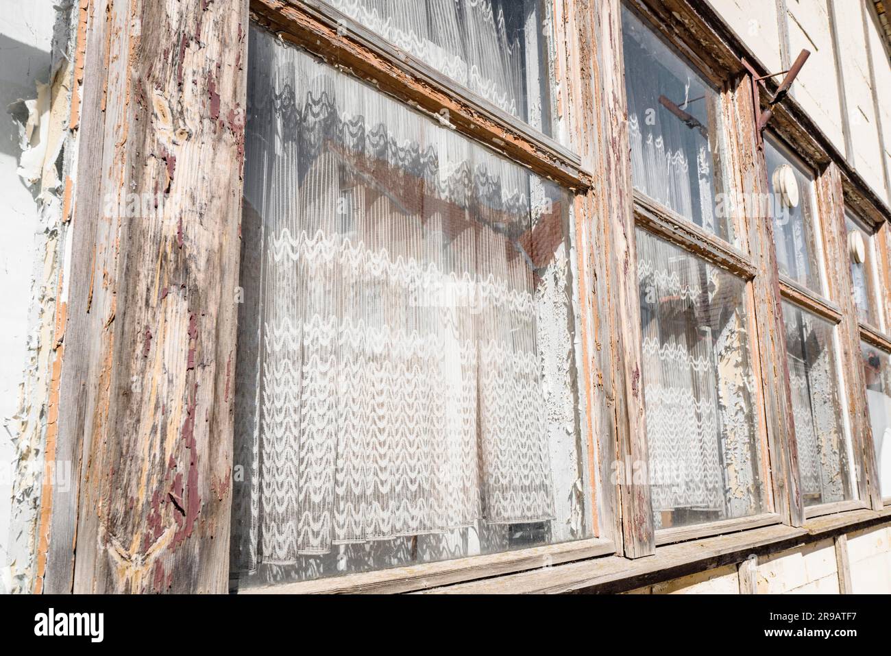 Old wooden windows on a row with white vintage curtains in a village ...