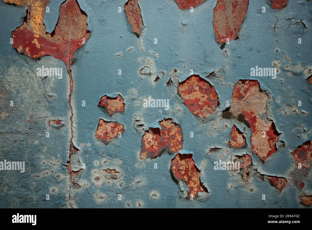 Weathered blue wall with pealing paint on a rusty surface in red color ...