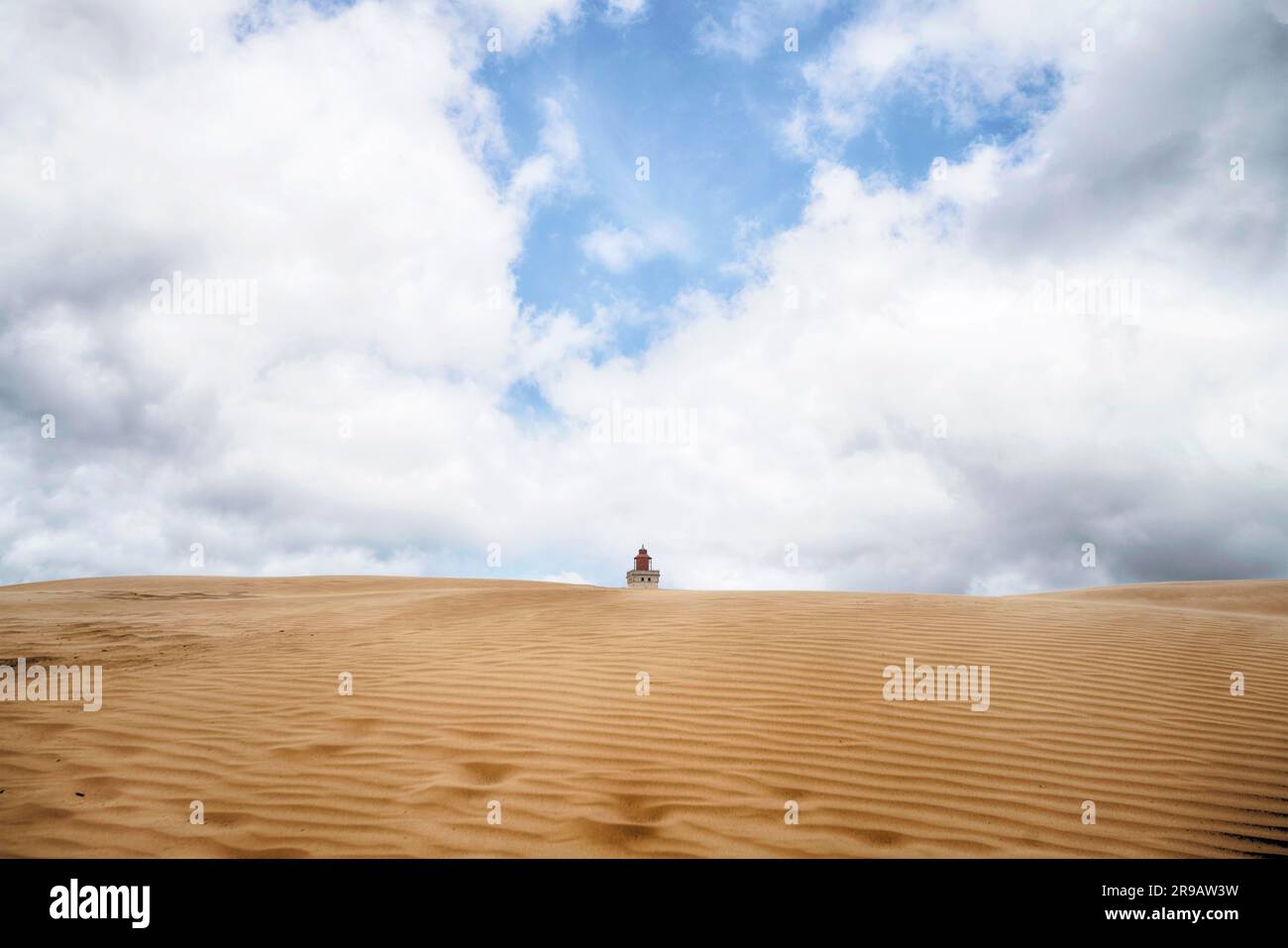 Lighthouse buried in a large sand dune under a blue cloudy sky in a ...