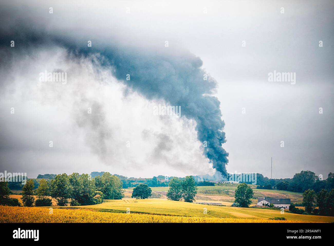 Black smoke from a fire in a rural countryside landscape with fields ...