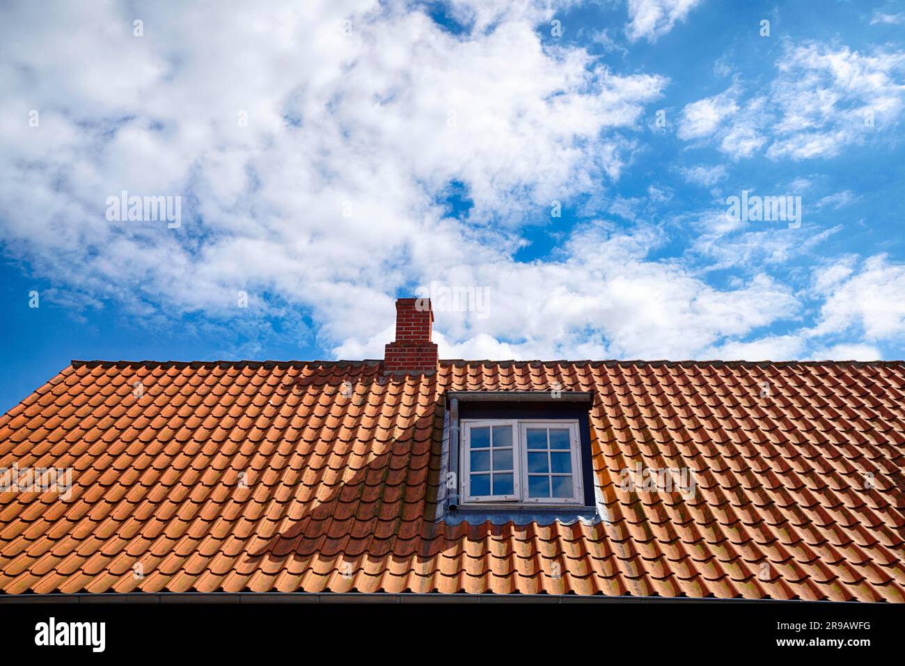 Tiled red roof with a rooftop window and a small chimney under a blue ...